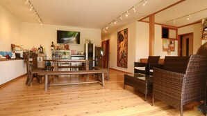 Uma sala ampla com piso de madeira, uma mesa de jantar, móveis de vime e uma cozinha equipada, incluindo uma geladeira.