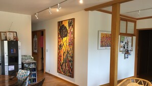Um quarto espaçoso com piso de madeira, uma mesa de jantar com cadeiras, uma geladeira e um grande quadro abstrato na parede.