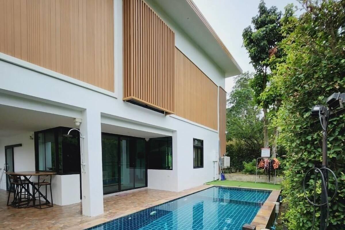 Uma casa moderna com piscina, um alpendre com mobiliário de exterior e um jardim bem cuidado.