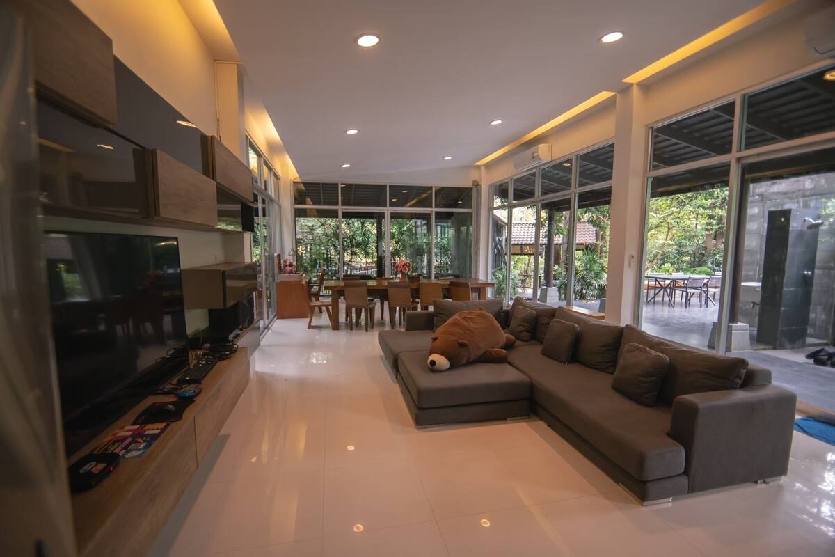 Uma sala de estar moderna com sofá seccional, TV de tela plana e área de jantar com mesa e cadeiras.