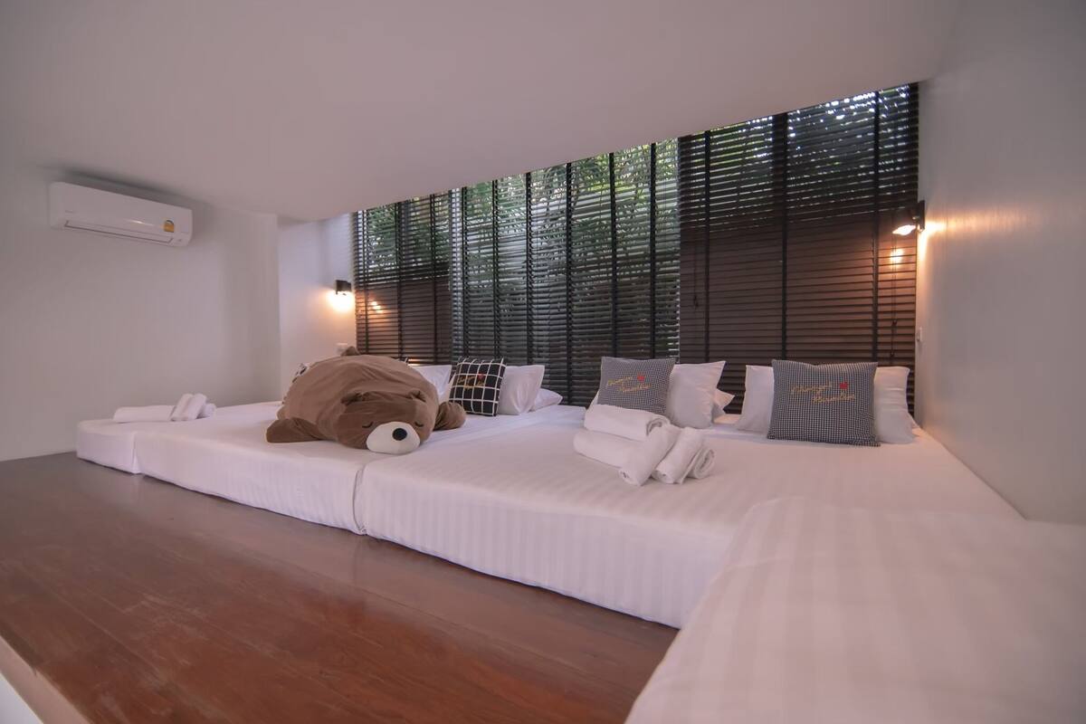 Quarto de hotel moderno com uma cama grande, um urso de pelúcia e uma janela com persianas.