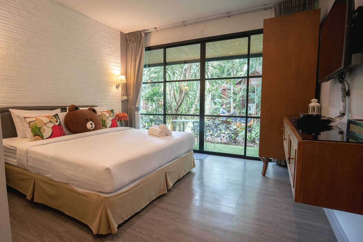 Quarto de hotel com uma cama grande, uma cômoda de madeira e vista para um jardim através de uma janela ampla.