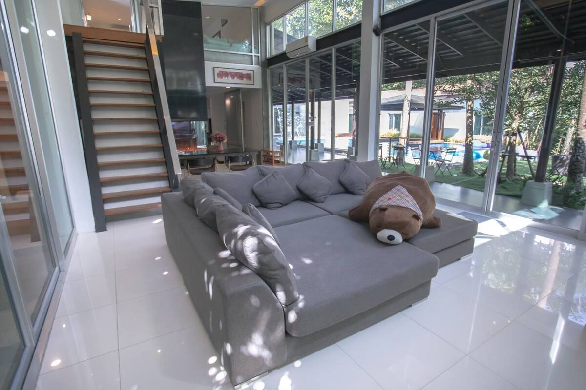 Uma sala de estar moderna com um sofá seccional cinza, um urso de pelúcia grande e uma escada que leva a um andar superior.