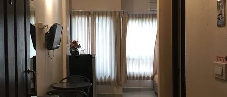 Quarto de hotel com área de refeições, televisão fixada na parede e janela com cortinas.