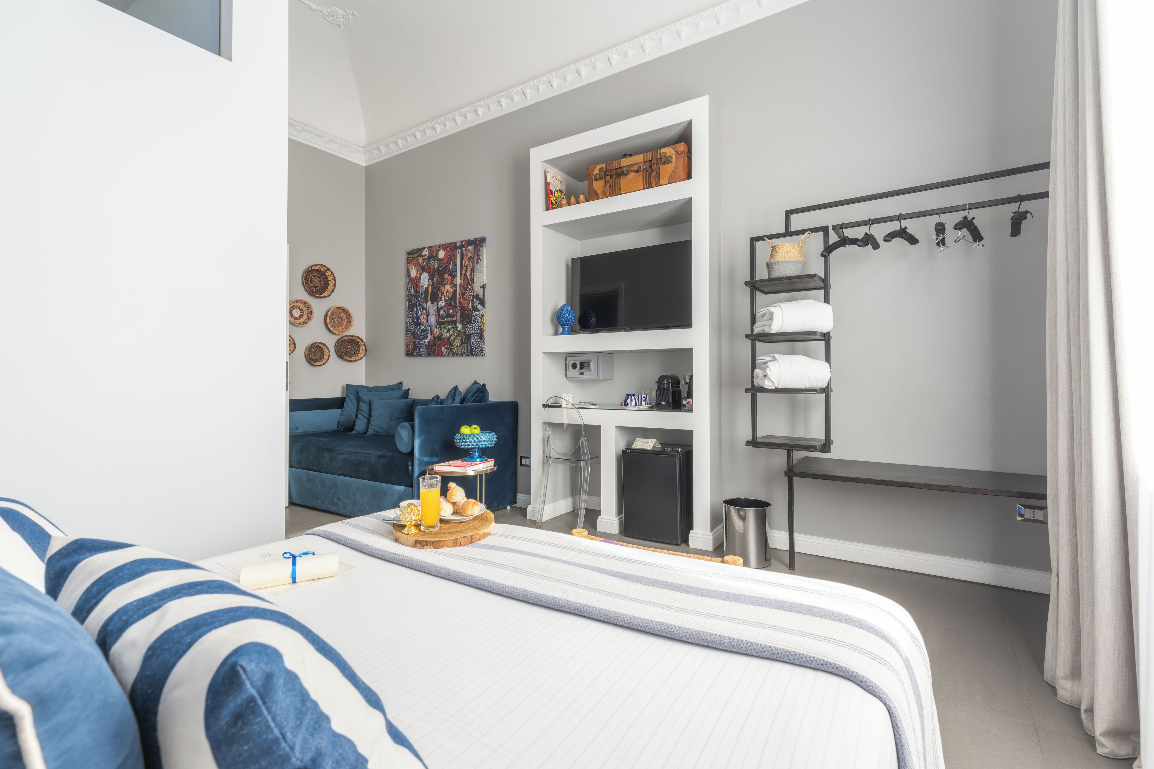 Quarto moderno com cama, pequeno espaço de cozinha, guarda-roupa e área de estar com sofá.