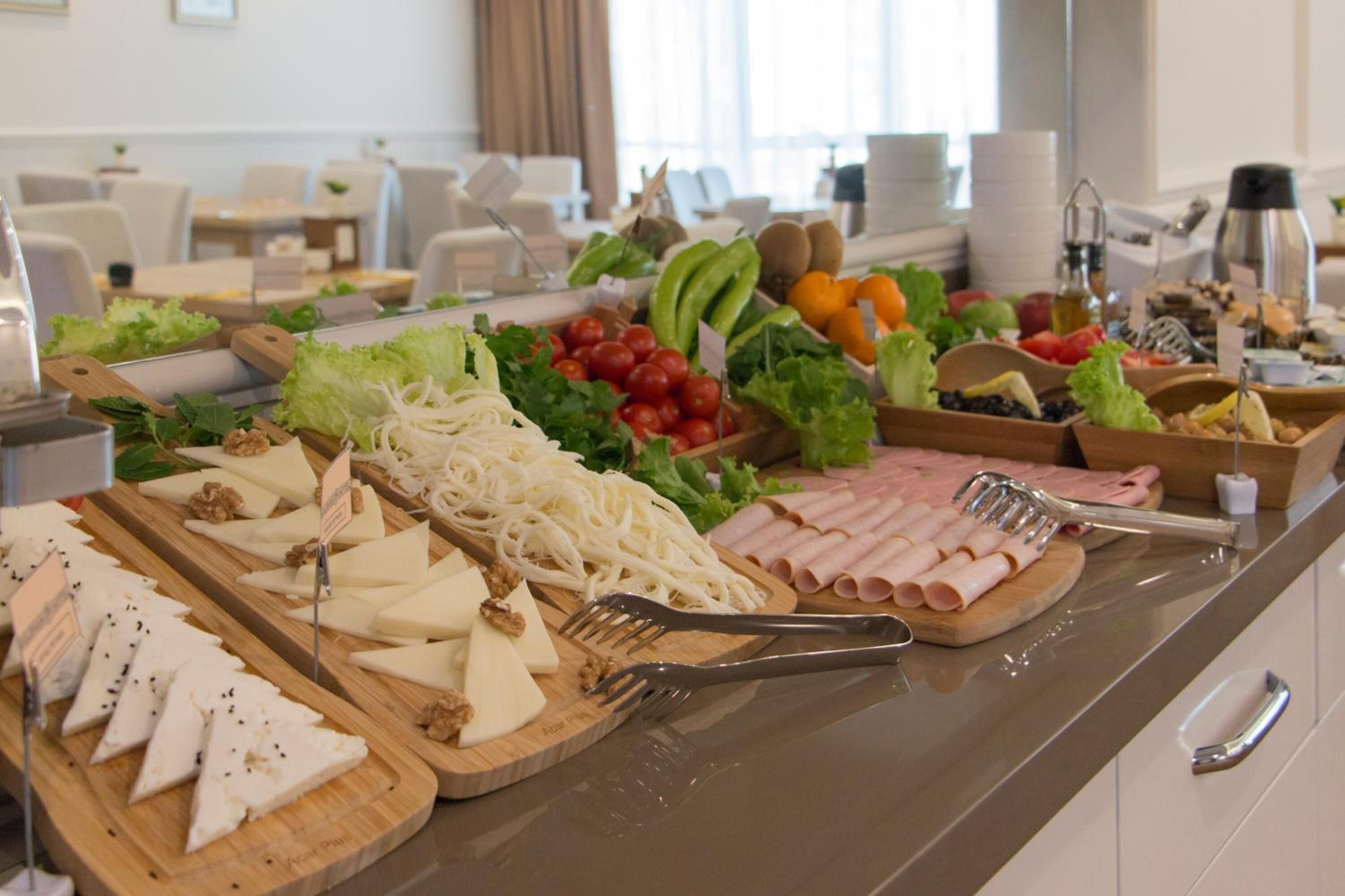 Um buffet com diversos queijos, carnes, frutas e legumes.