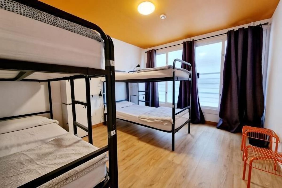 Quarto com beliches, uma cadeira e janela com cortinas.