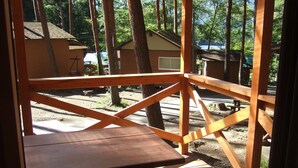 Um deck de madeira com uma mesa de piquenique, rodeado por árvores e um pequeno edifício ao fundo.