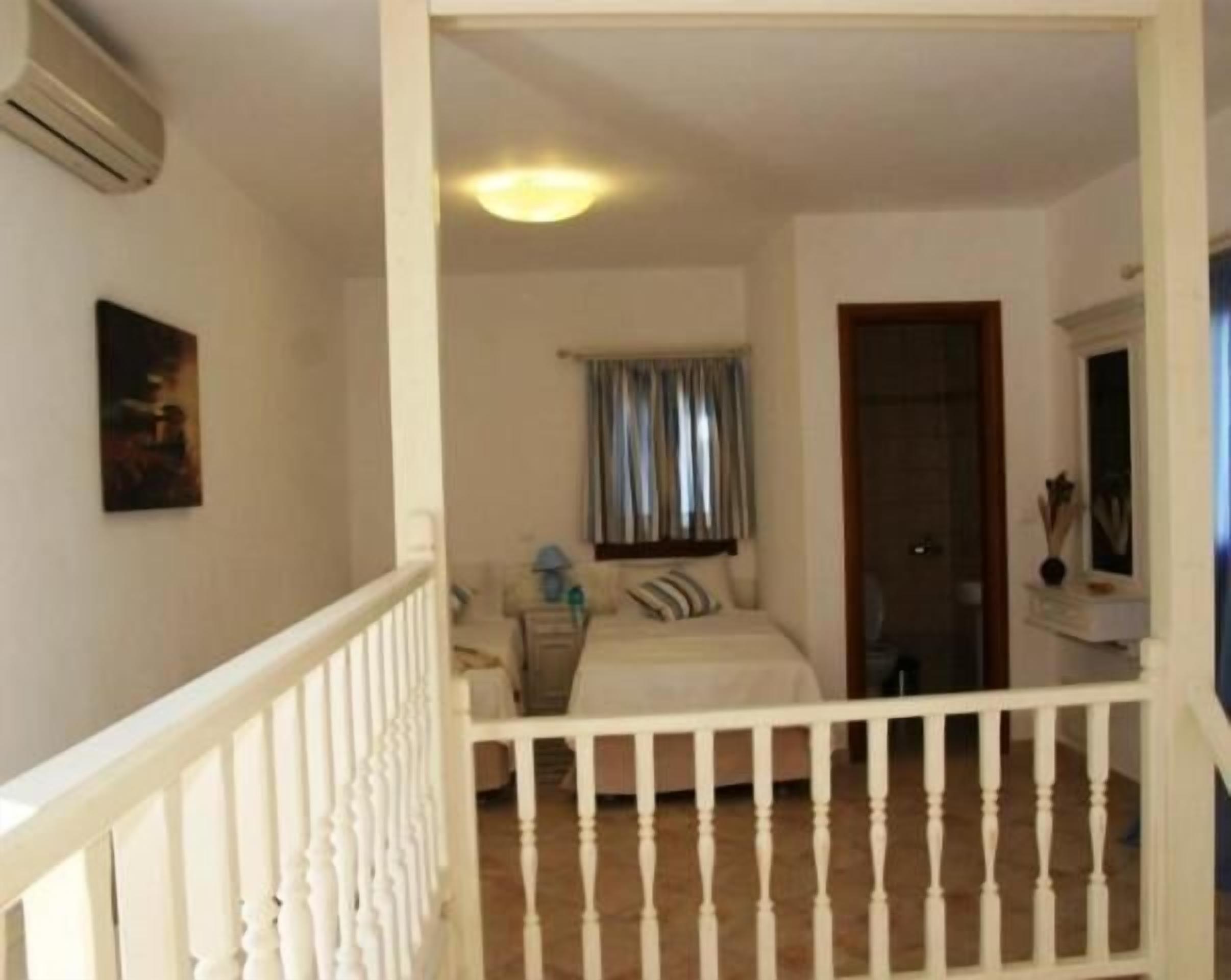 Um quarto com uma cama, uma janela com cortinas, uma mesinha de cabeceira e uma porta.