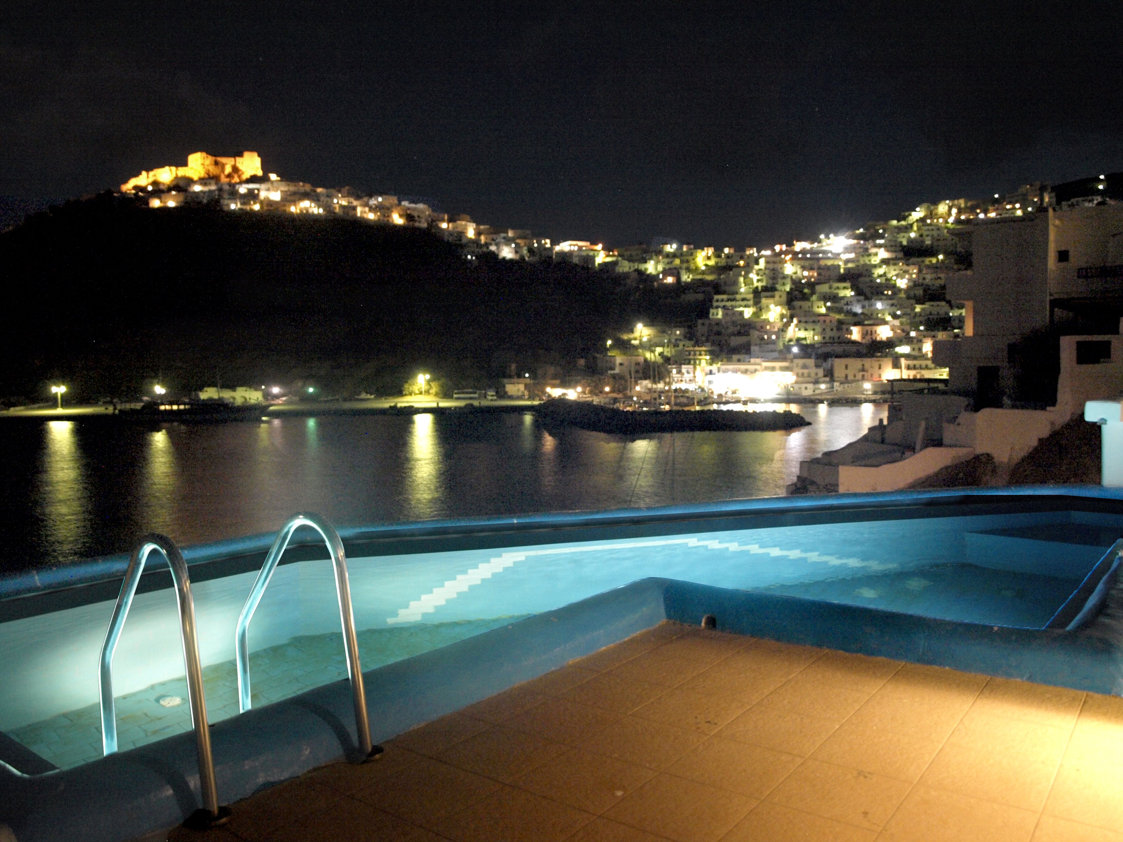 Piscina com degraus de acesso, com vista para um corpo de água e uma colina ao fundo.