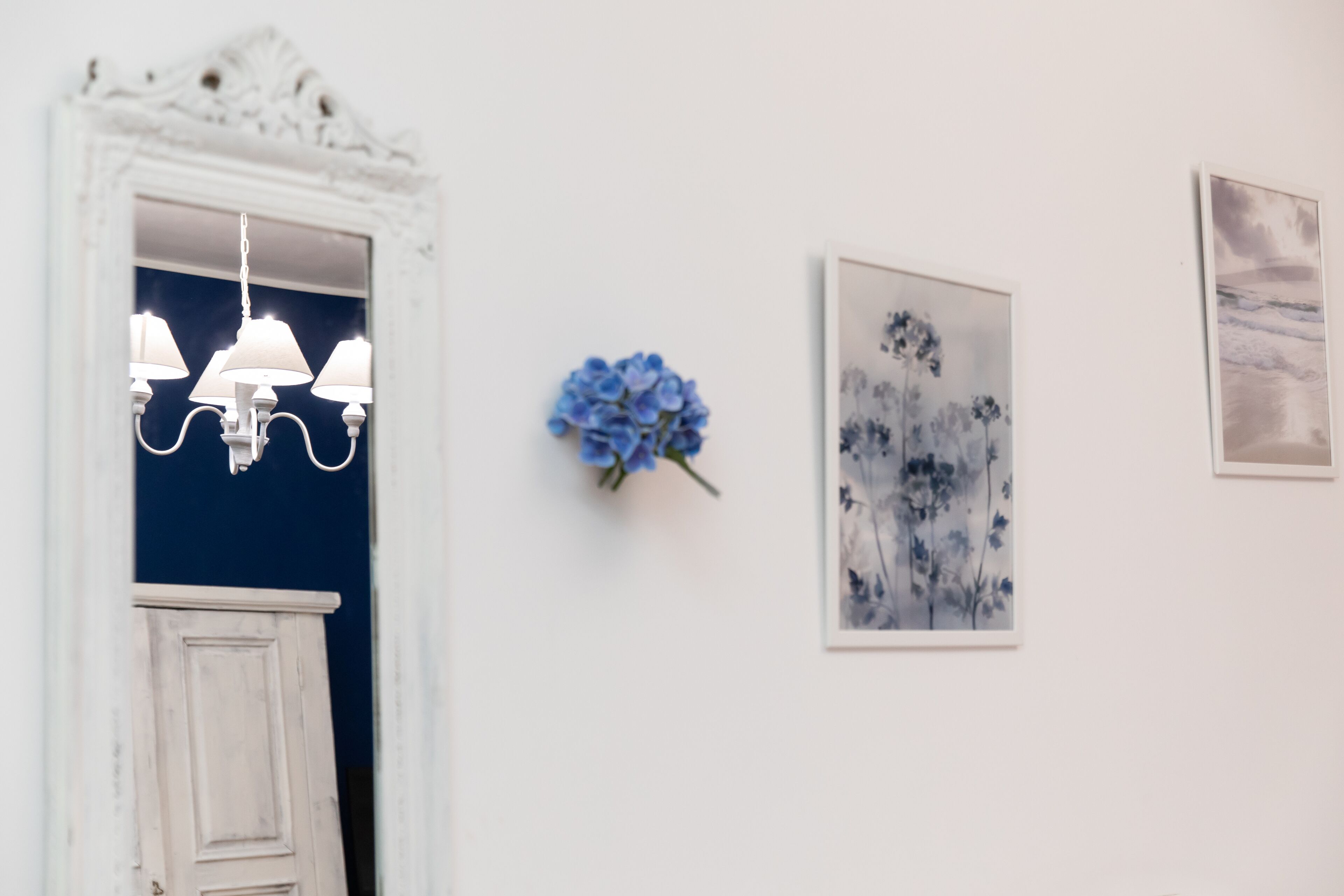 Quarto com porta branca, parede azul e um candelabro. Há duas obras de arte emolduradas na parede.