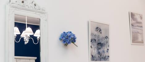 Quarto com porta branca, parede azul e um candelabro. Há duas obras de arte emolduradas na parede.