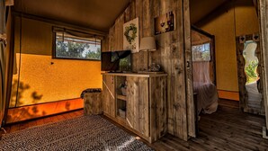 Quarto rústico com paredes de madeira, uma cama com dossel, uma mesinha com abajur e uma janela com vista para árvores.