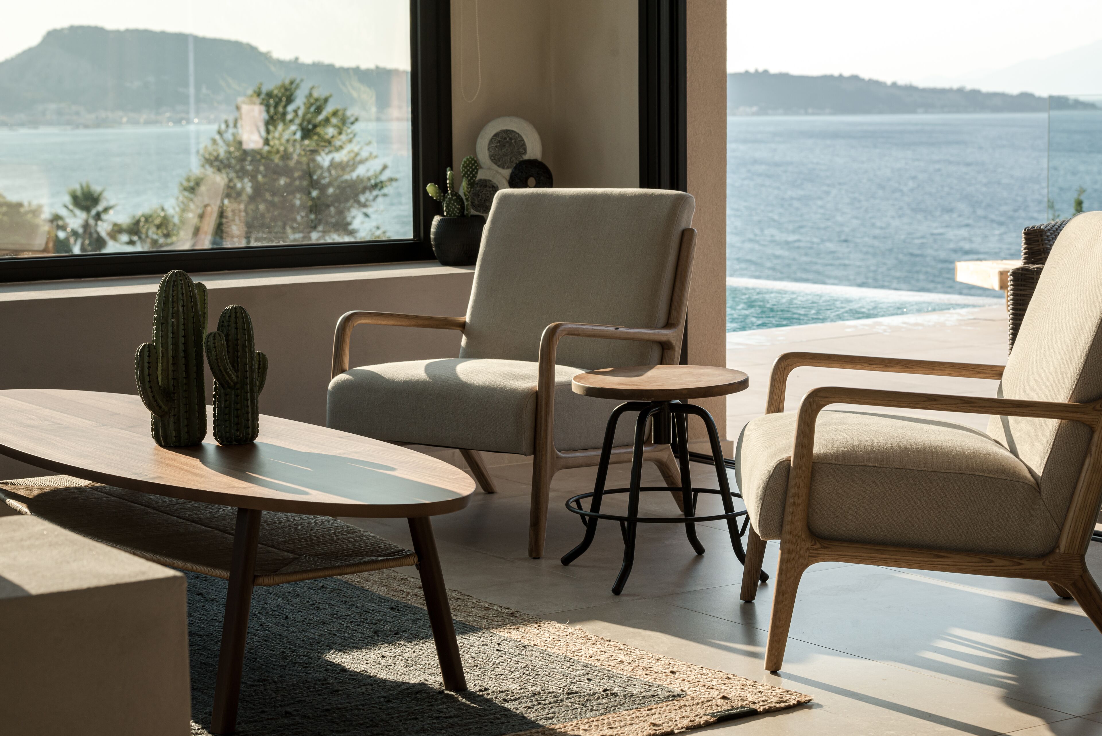 Sala de estar moderna com vista para o mar, com uma mesa redonda, duas poltronas e um banquinho.