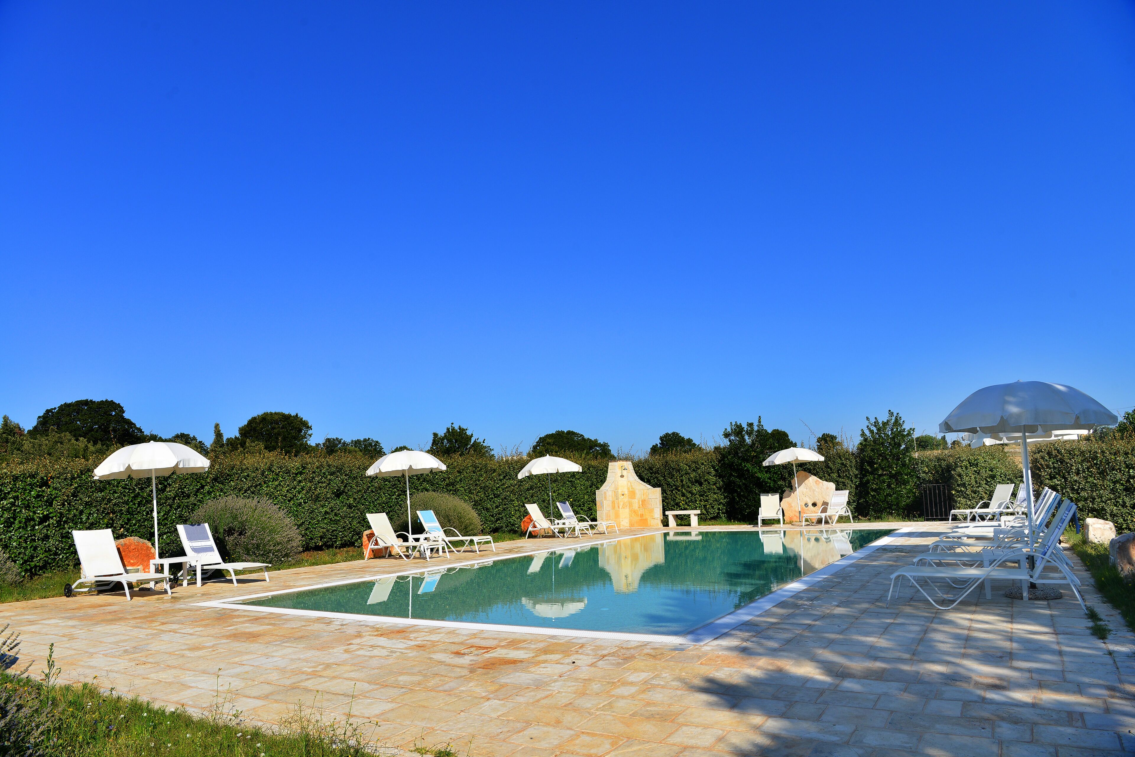 Uma área de piscina com espreguiçadeiras e guarda-sóis, rodeada por vegetação e um céu claro.
