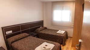 Quarto de hotel com duas camas, piso de madeira, janela com persianas e uma porta.