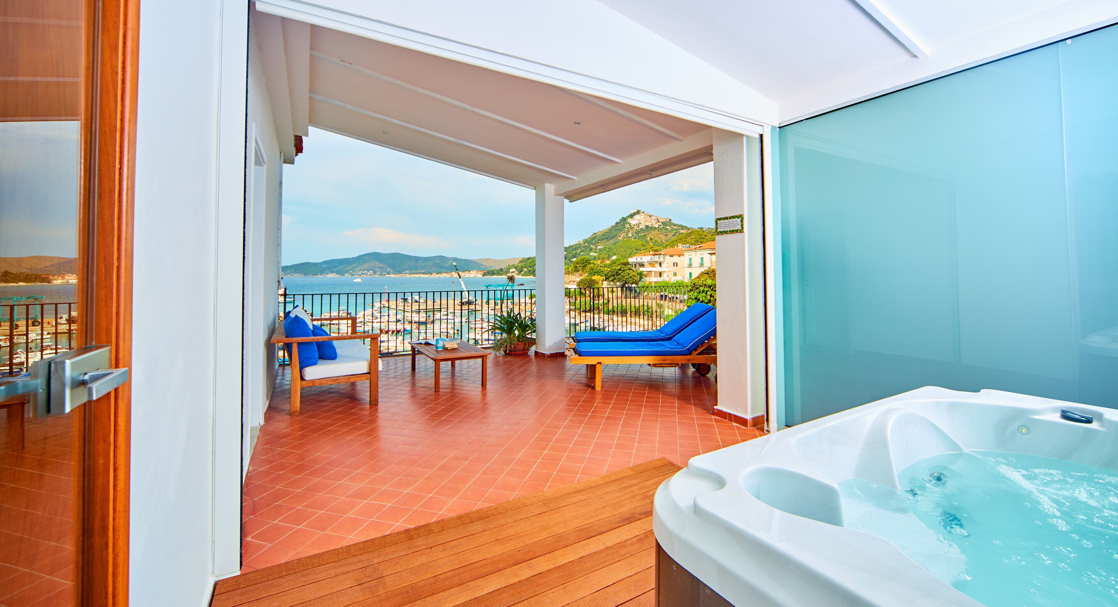Uma varanda com vista para o mar, uma banheira de hidromassagem e um espaço de estar com almofadas azuis.