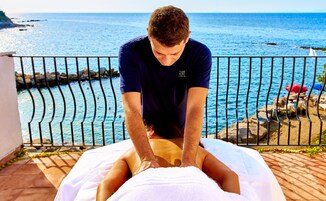 Uma pessoa recebendo massagem nas costas em uma varanda com vista para o mar.