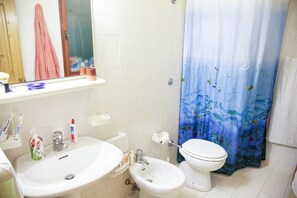 Um banheiro com pia, bidê, vaso sanitário e cortina de chuveiro com desenho de peixe.