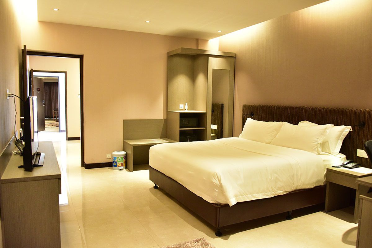 Quarto de hotel com uma cama grande, mesas de cabeceira, um guarda-roupa e uma escrivaninha com uma cadeira.
