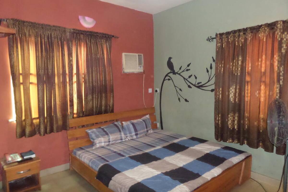 Quarto com cama de madeira, mesa de cabeceira, ar-condicionado fixado na parede e um objeto decorativo na parede.