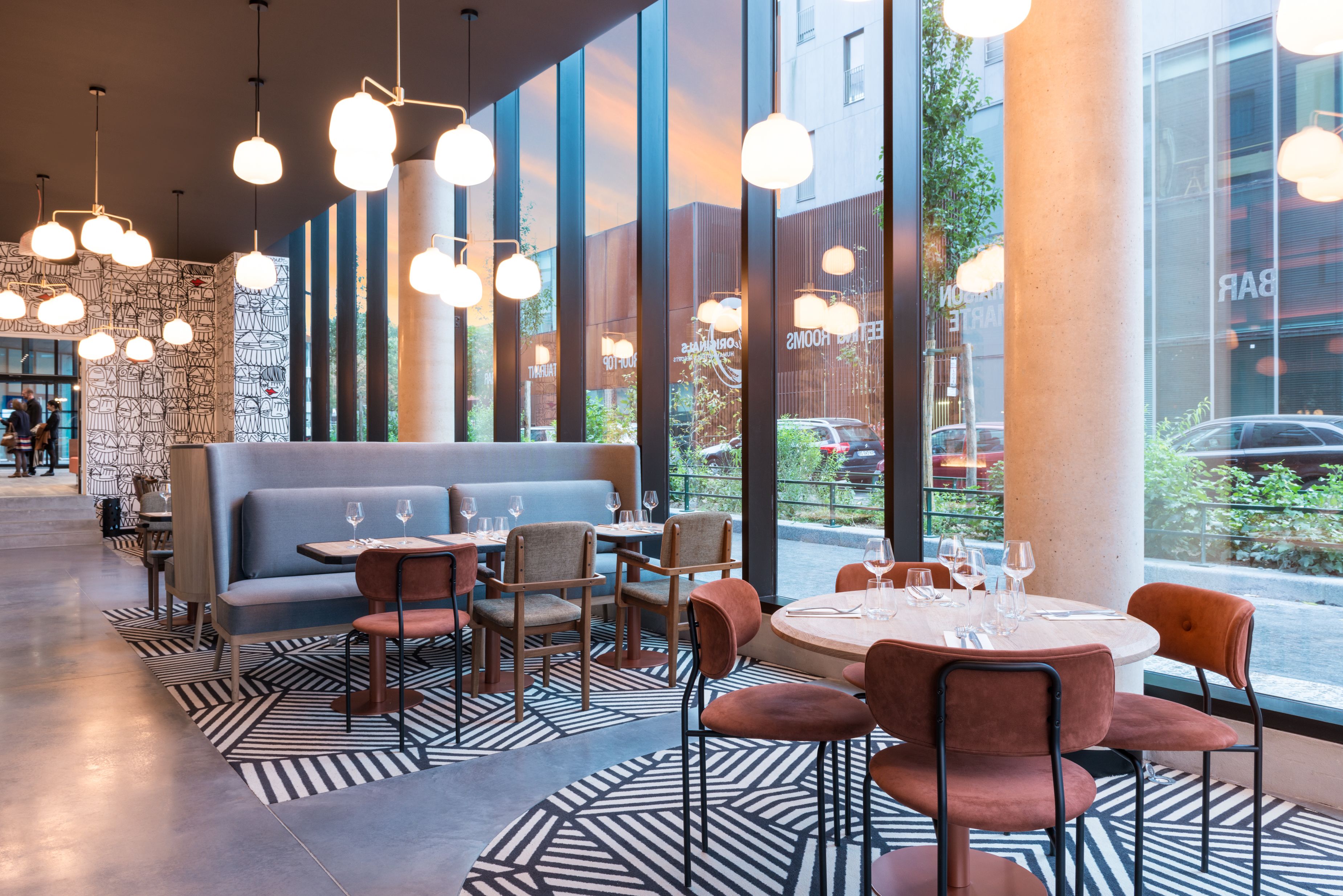 Interior de restaurante moderno com diferentes opções de assento, incluindo um sofá e mesas redondas, e um chão com padrão.