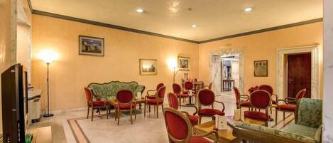 Um saguão de hotel com várias áreas de estar, incluindo sofás e poltronas, uma televisão e obras de arte emolduradas nas paredes.