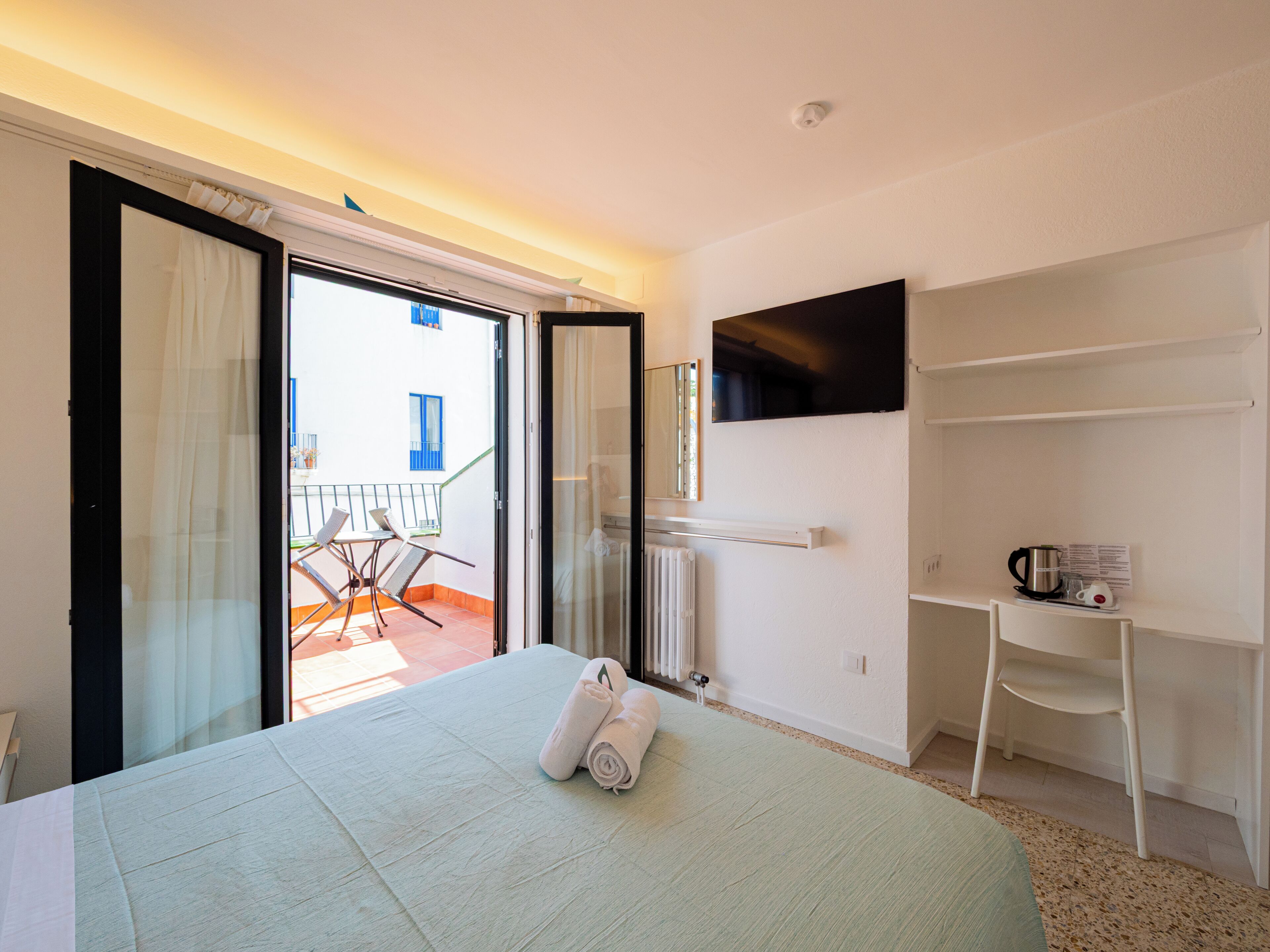 Quarto de hotel com cama, escrivaninha, cadeira, televisão e vista para a varanda.