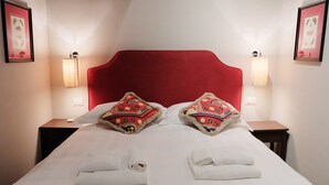 Cama bem arrumada com cabeceira vermelha e almofadas decorativas, lençóis brancos e duas mesas de cabeceira com abajures.