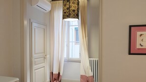 Um corredor com uma porta branca, um radiador e uma janela com cortinas leves.