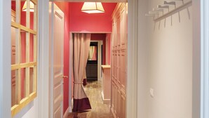 Um corredor com piso de madeira, parede vermelha e porta que dá para um quarto.