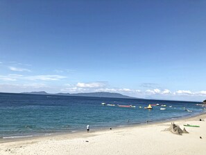 Uma praia com céu claro, águas calmas e montanhas ao longe.