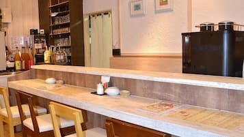 Uma cozinha com bancada comprida, banquetas, armários de madeira e máquina de café.