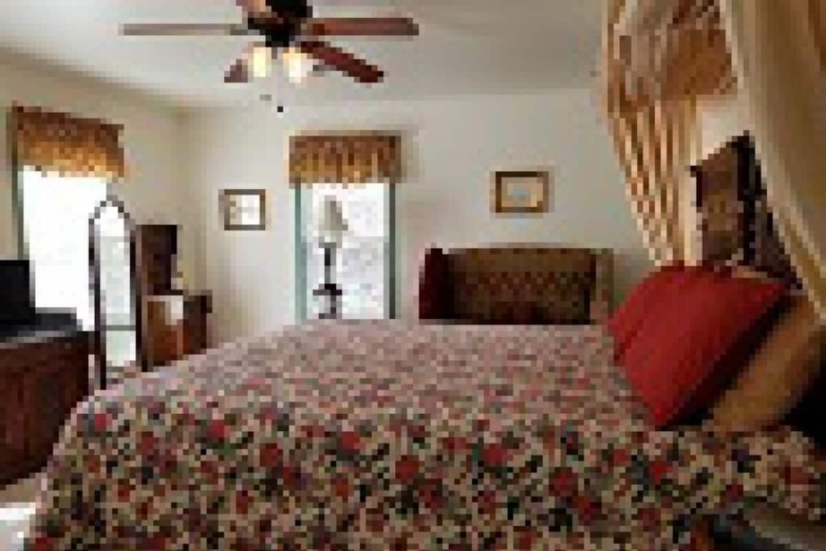 Quarto com cama, ventoinha no teto e janela com cortinas.