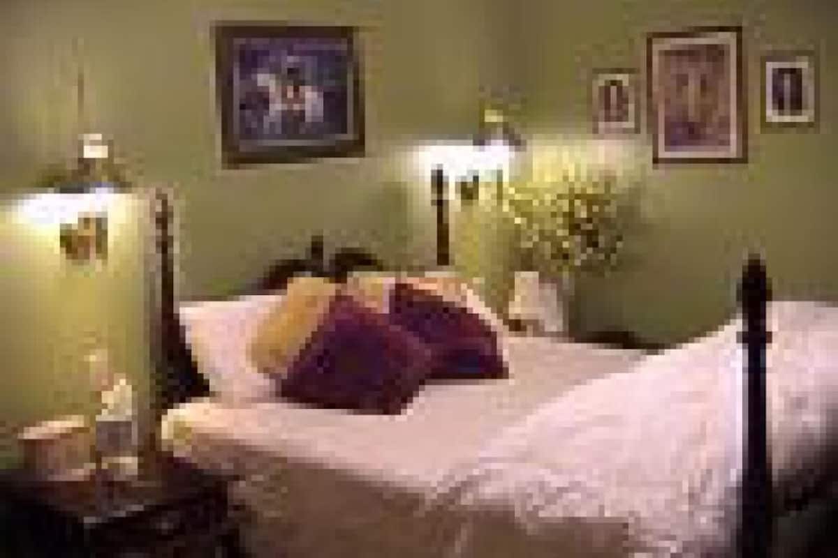 Quarto com cama, mesas de cabeceira e luminárias fixadas na parede.