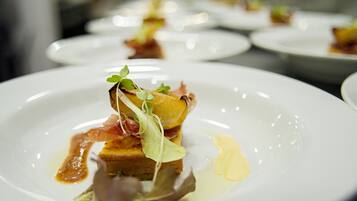Um close-up de um prato gourmet em uma placa branca, com molho e vegetais verdes.