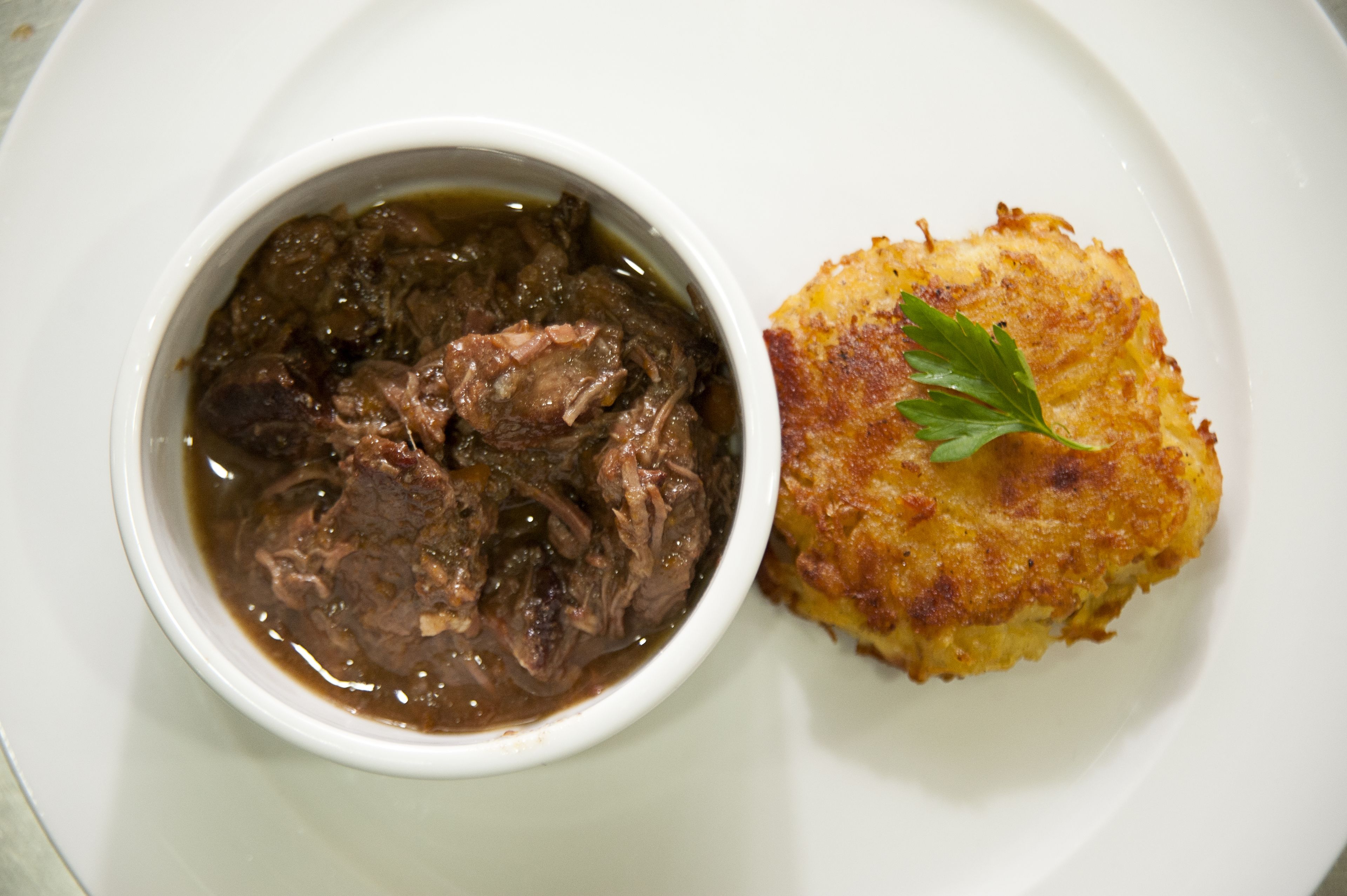 Um prato branco com um tigela de ensopado marrom escuro e um bolinho de batata dourado, decorado com uma folha.