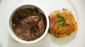 Um prato branco com um tigela de ensopado marrom escuro e um bolinho de batata dourado, decorado com uma folha.