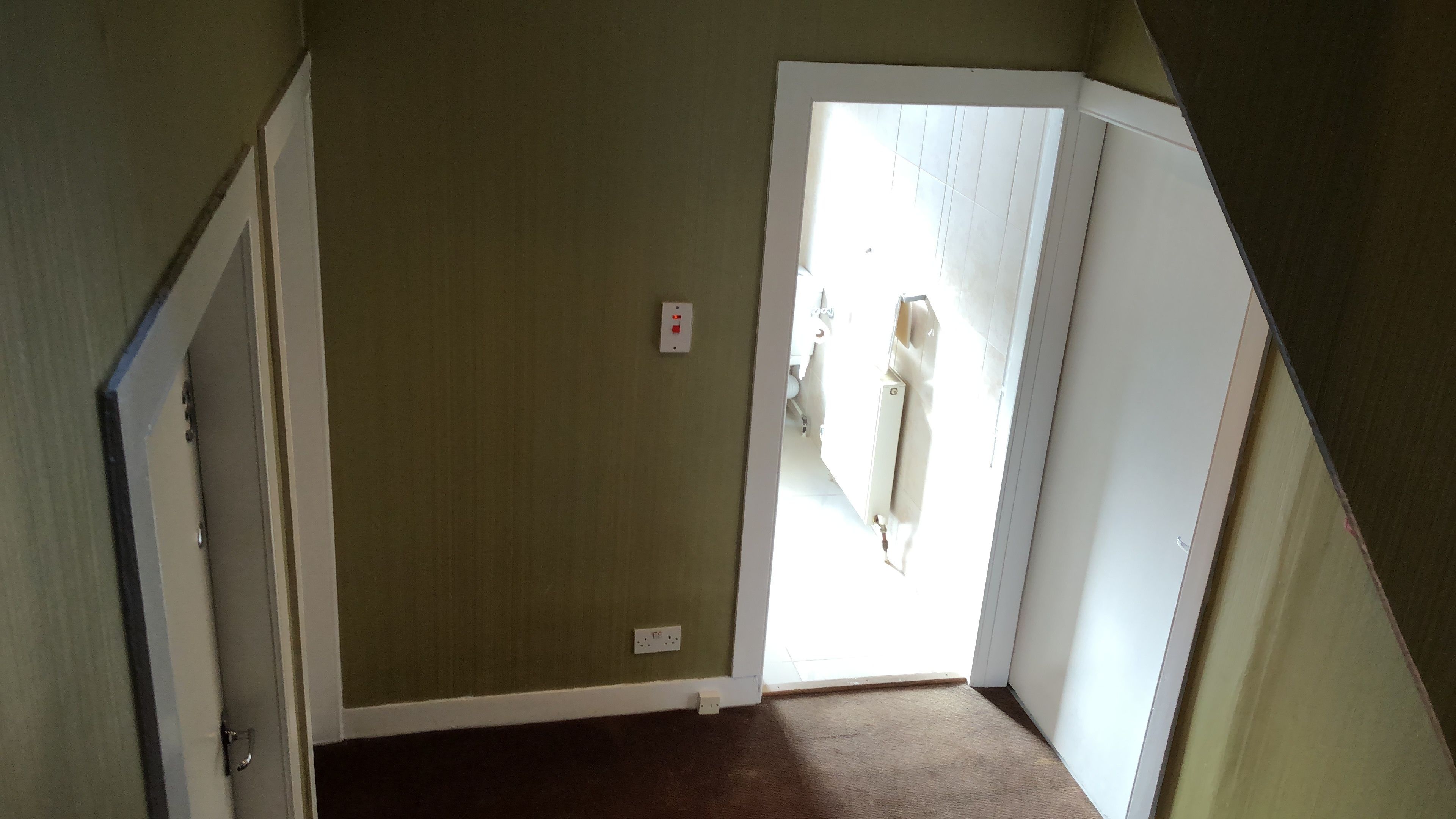 Um corredor estreito com uma porta que dá para um quarto claro.