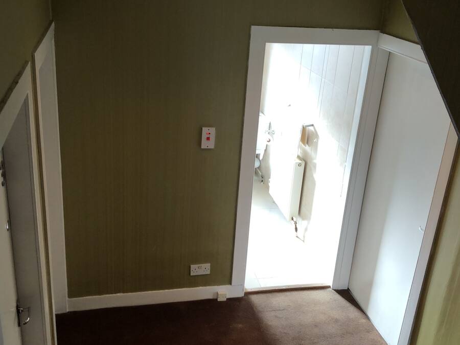 Um corredor estreito com uma porta que dá para um quarto claro.