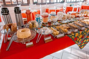 Uma mesa de buffet com diversos alimentos e utensílios, incluindo bolo, doces e uma estação de café.