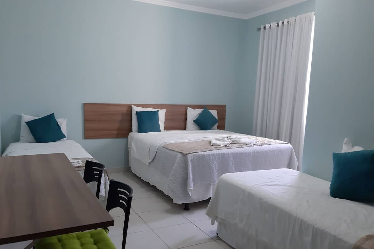 Quarto de hotel com duas camas, uma mesa de jantar e uma cadeira.