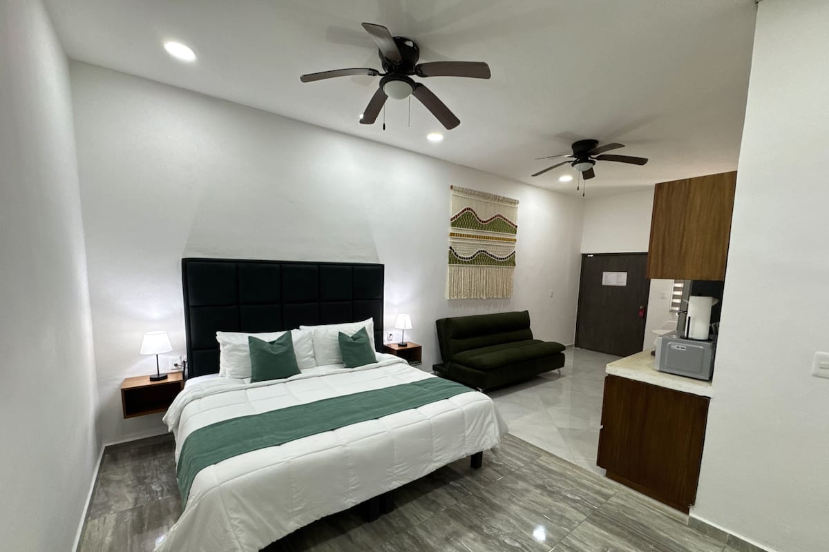 Quarto de hotel moderno com uma cama grande, um sofá, uma kitchenette e dois ventiladores de teto.