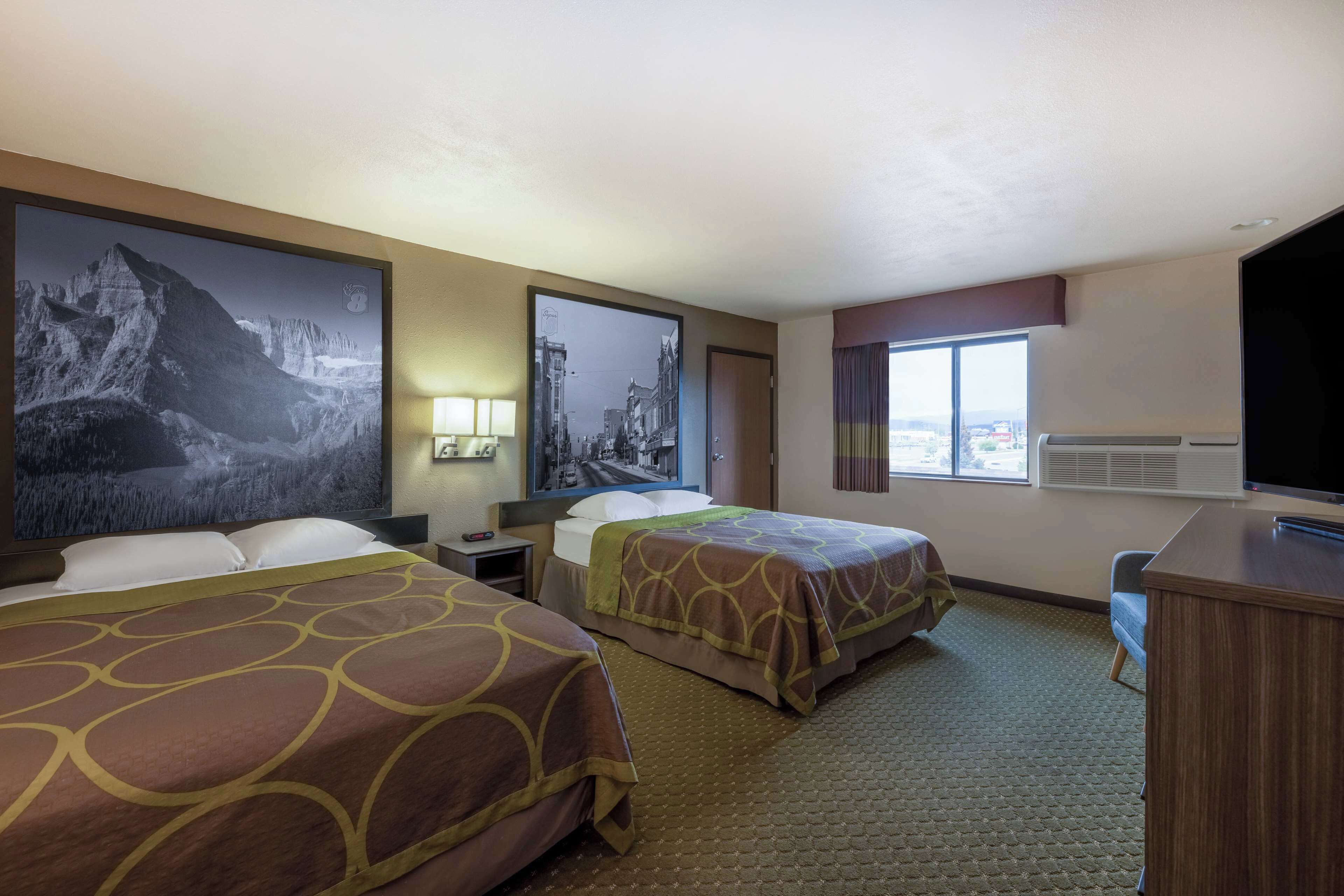 Quarto de hotel com duas camas, uma escrivaninha, televisão e amplas janelas com vista.