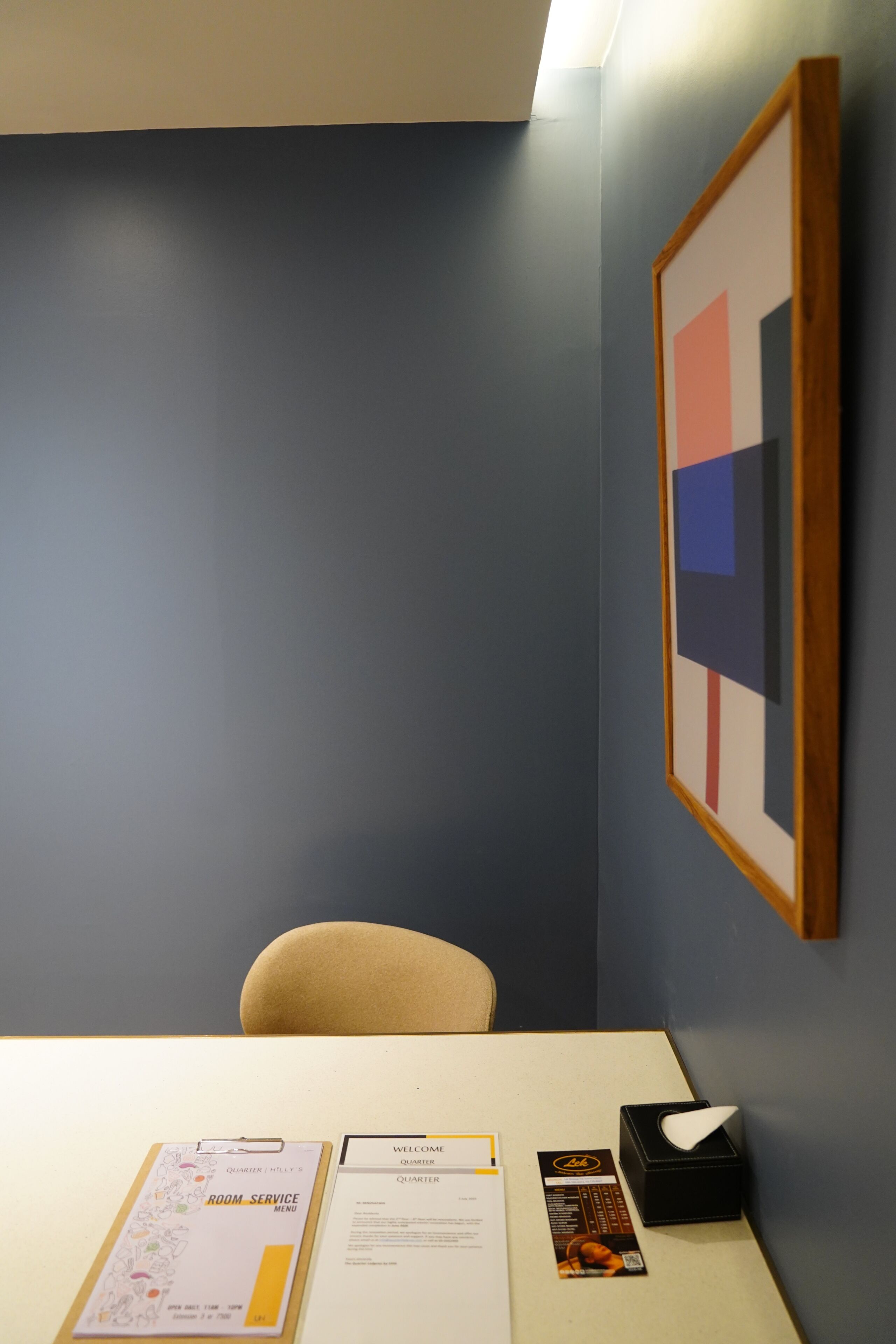 Quarto de hotel com uma escrivaninha, um quadro abstrato emoldurado, uma cadeira e uma caixa de lenços.