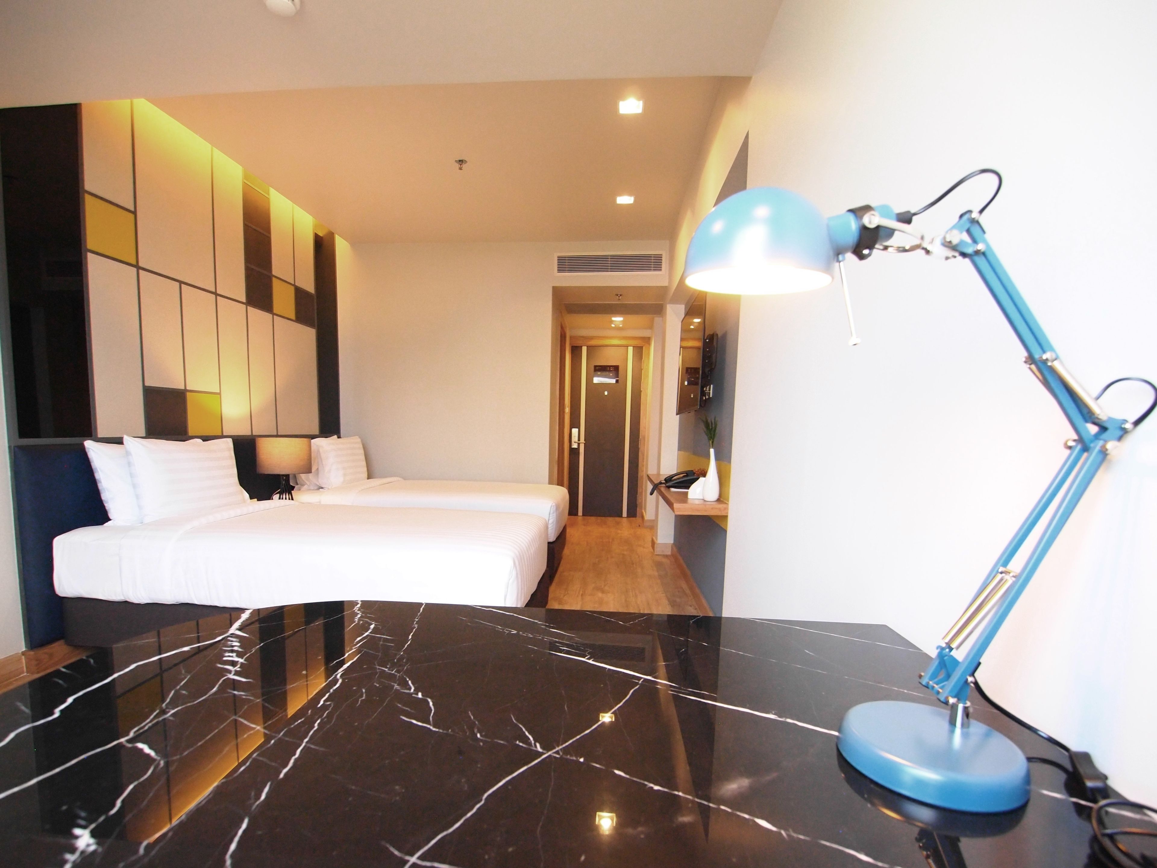 Quarto de hotel com uma cama grande, uma mesa com tampo de mármore e um abajur azul.