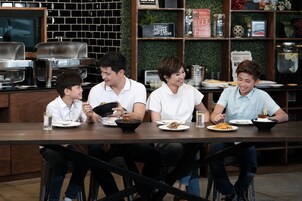 Um grupo de pessoas sentadas à mesa em um restaurante, com uma parede de tijolos e prateleiras ao fundo.
