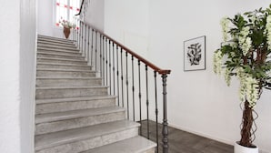 Escadaria com degraus de mármore e corrimão de madeira, conduzindo a um patamar com planta em vaso e obra de arte emoldurada na parede.