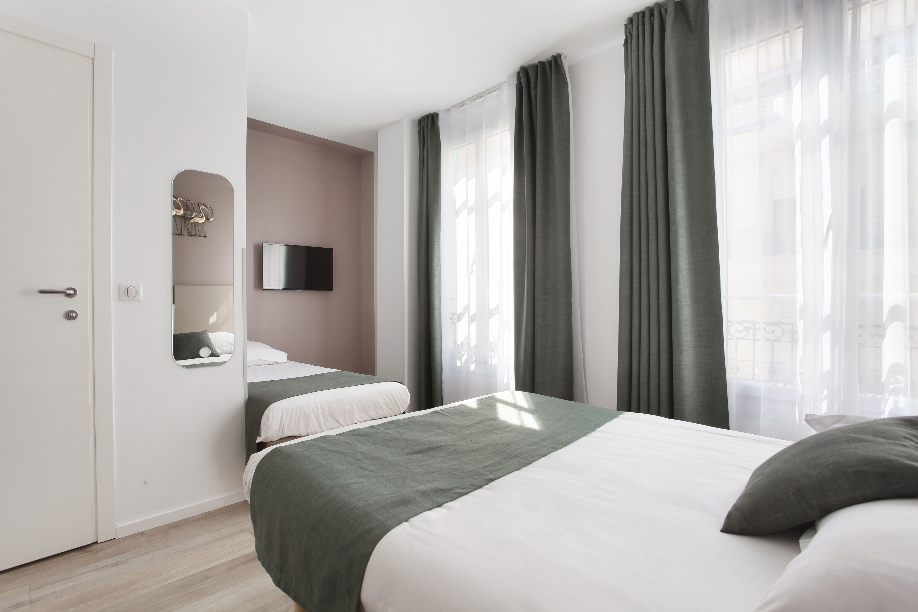 Quarto de hotel moderno com uma cama grande, um guarda-roupa, uma televisão e uma janela com cortinas.
