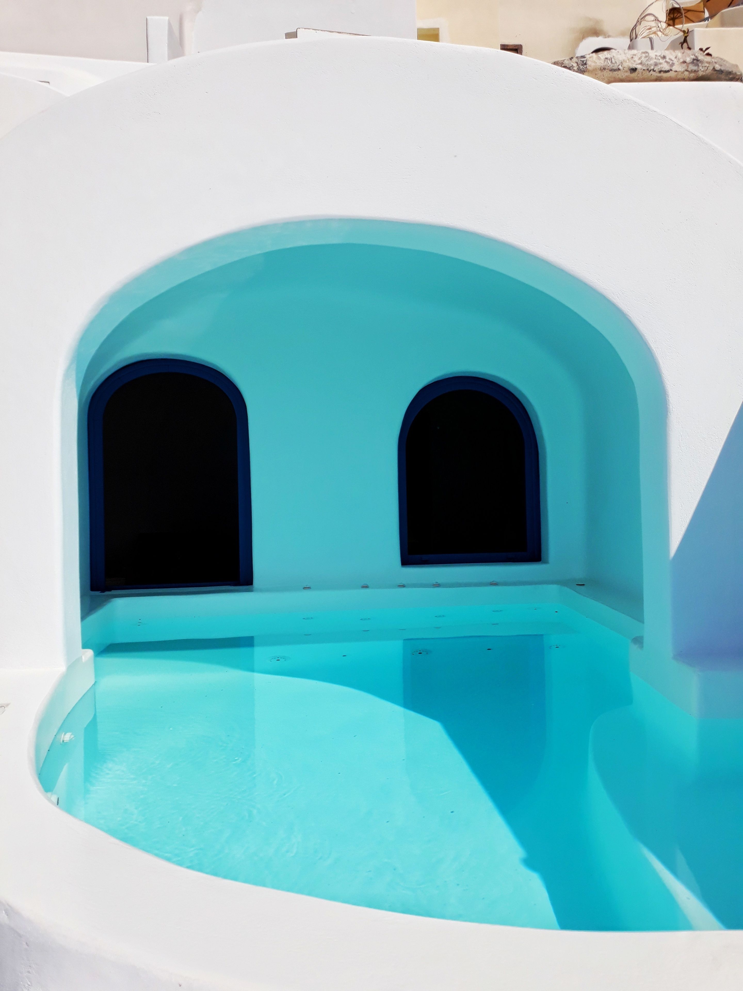 Um edifício branco com piscina turquesa e duas janelas em arco.